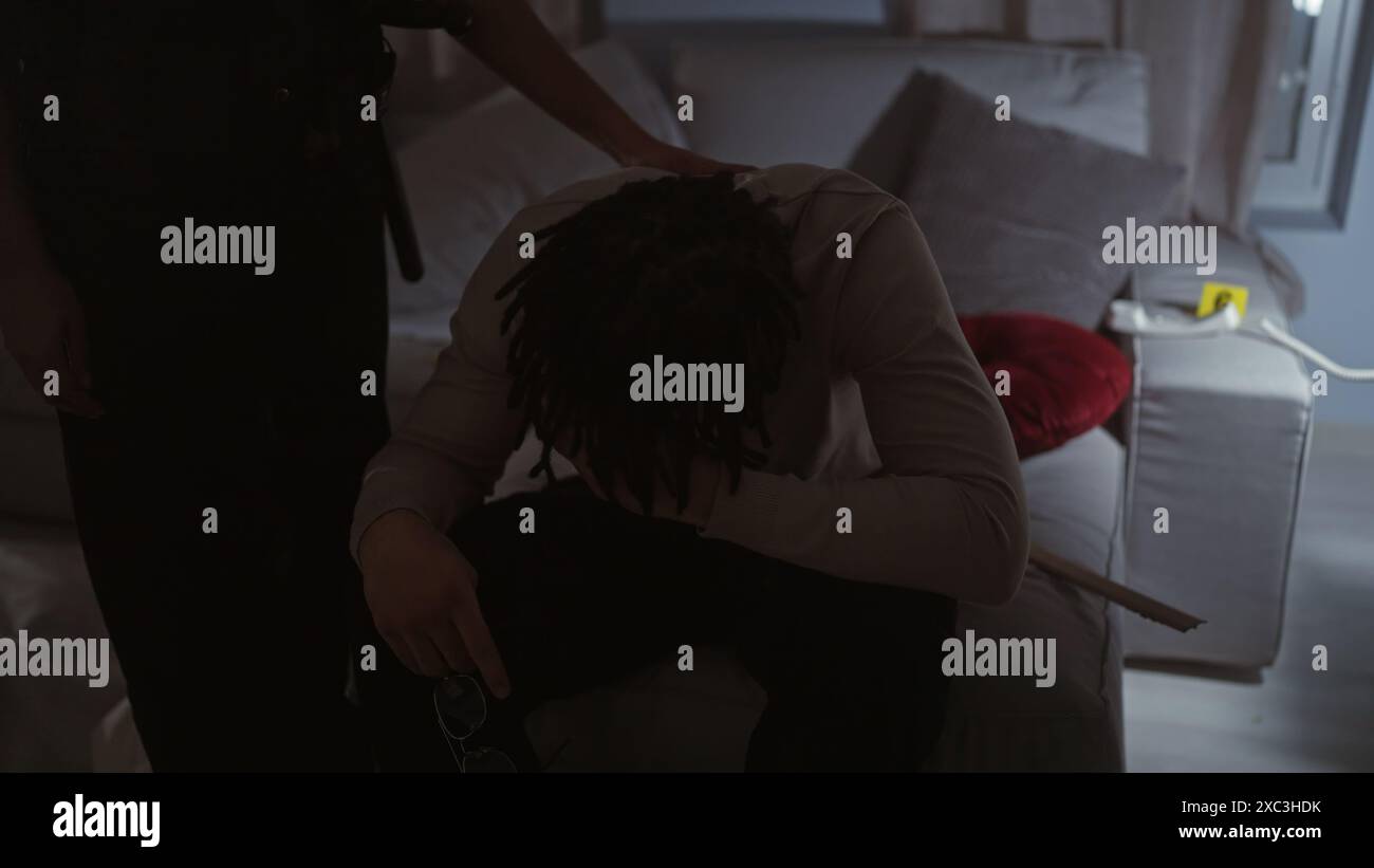 A handcuffed man seated indoors with a standing policewoman, portraying ...
