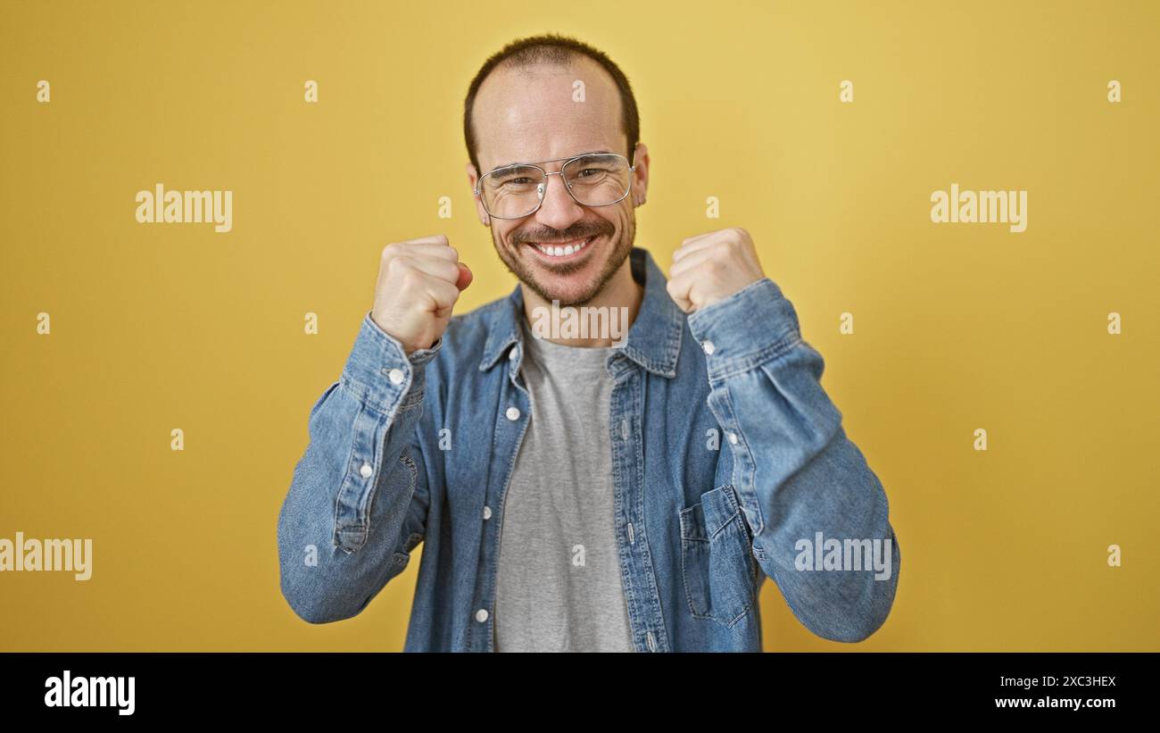Smiling bald hispanic man with beard, glasses, and denim jacket, making ...
