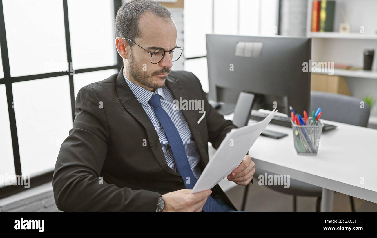 A focused businessman in glasses reads documents in a modern office ...