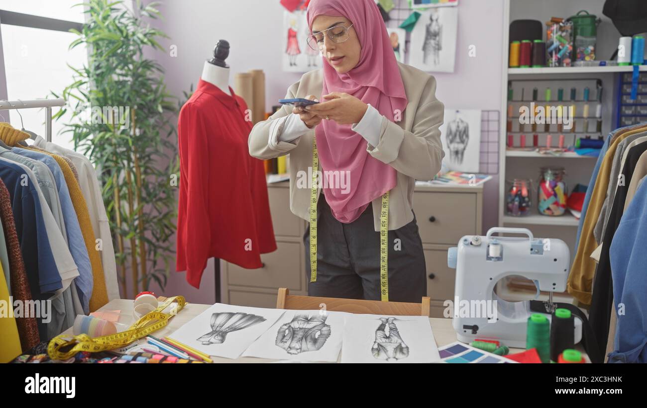 A young woman in a hijab takes photos of sketches in a busy tailoring ...