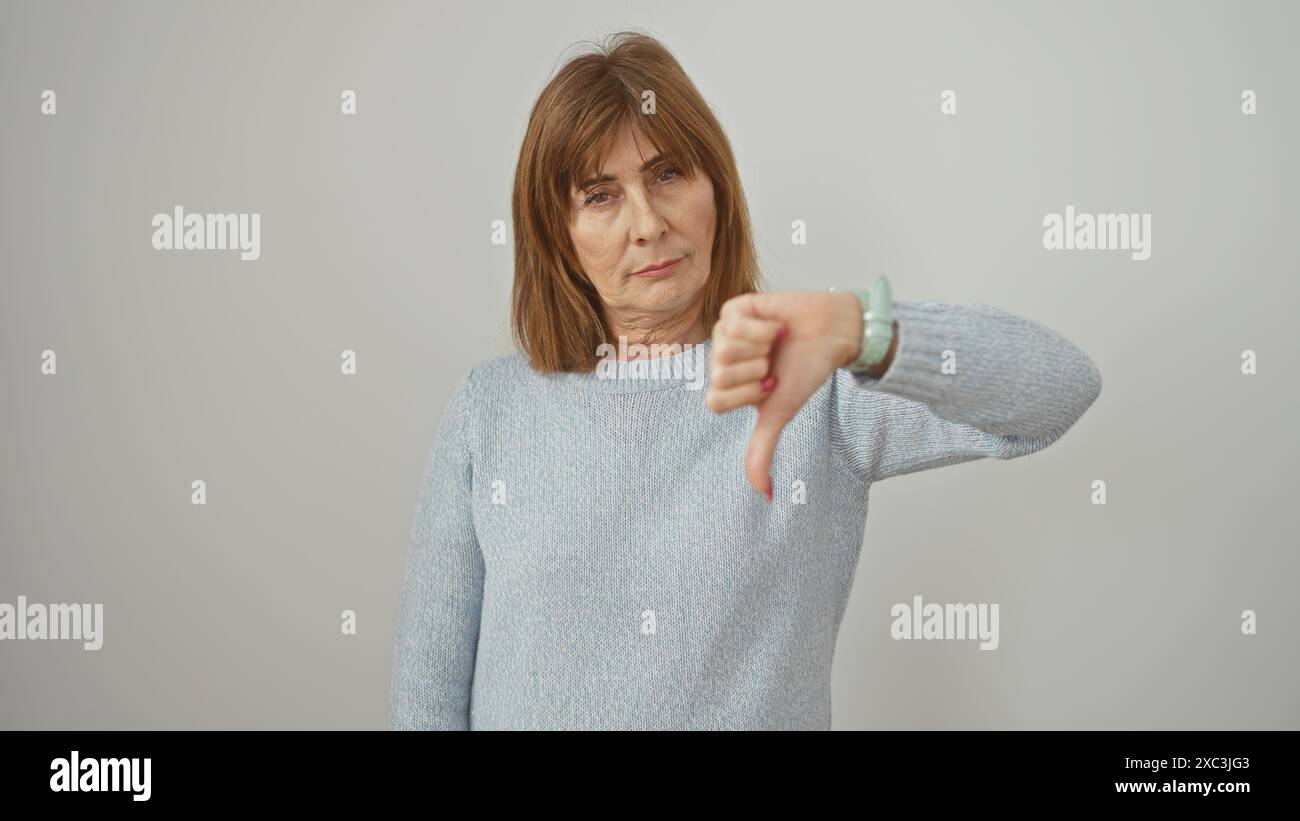 Middle-aged woman with short hair giving thumbs down against a white ...