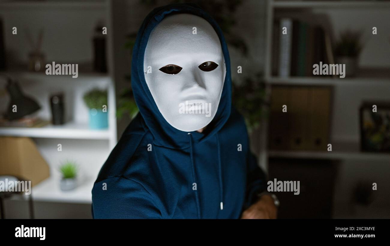 Masked man in hoodie posing in a modern office space, creating a ...