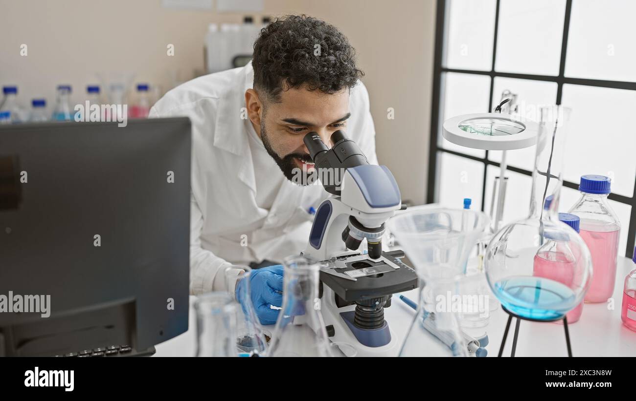 A young hispanic man with a beard examines samples using a microscope ...