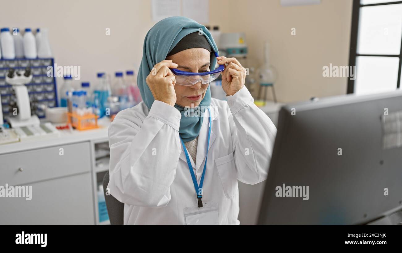 A woman in a hijab adjusts safety goggles in a laboratory setting ...