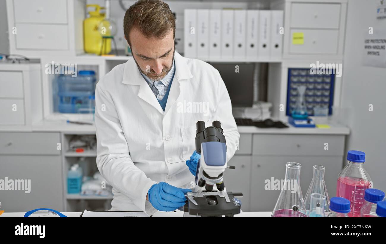 Middle-aged man in lab coat examines samples through a microscope in a ...