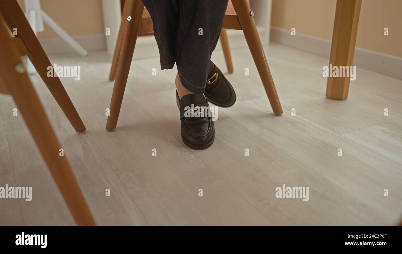 Close-up of a woman's feet wearing loafers beneath a wooden table on a ...