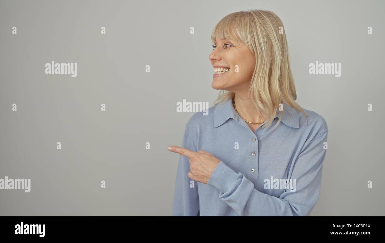 Smiling blonde woman points to something off-camera, against a white ...