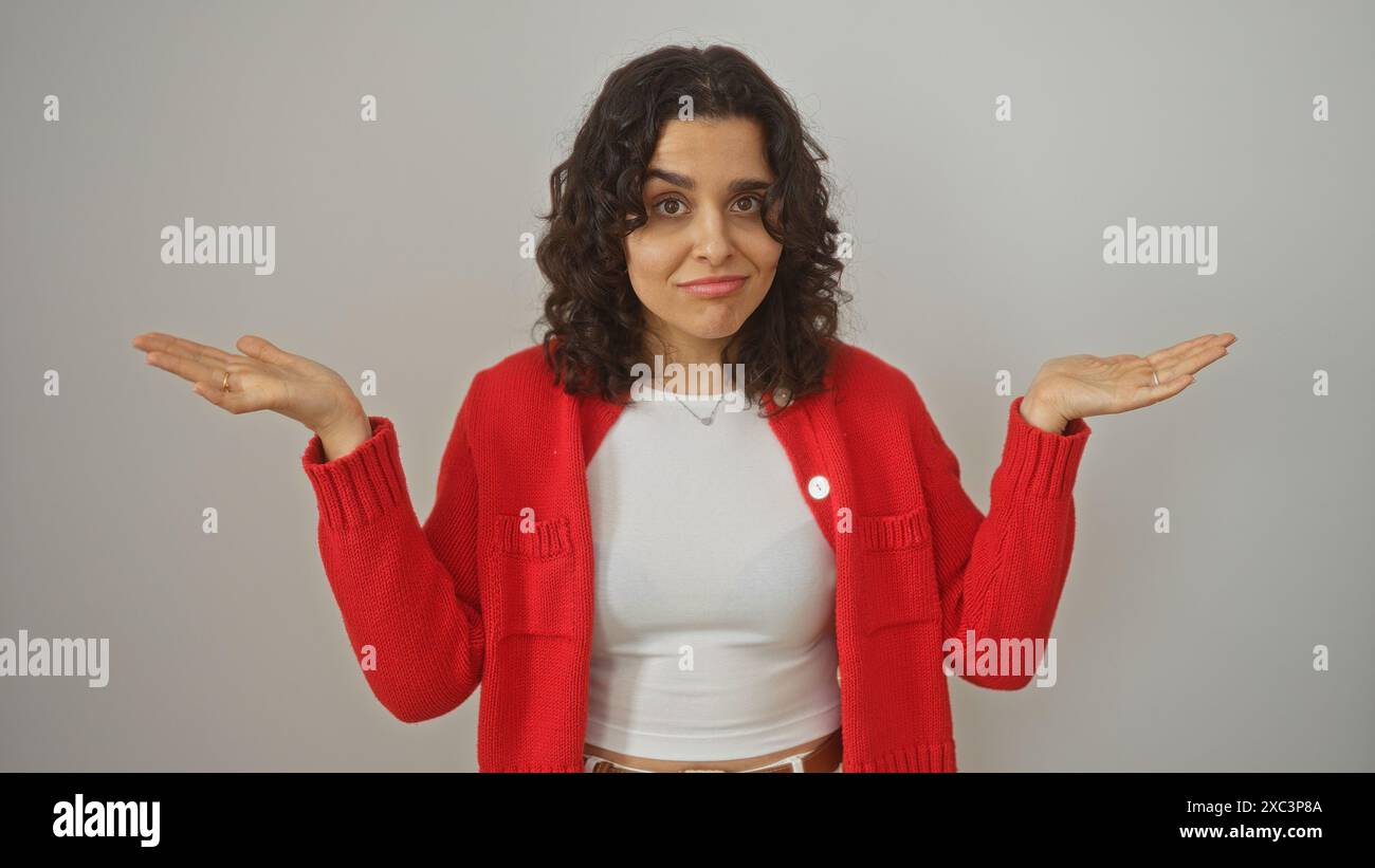 Young hispanic woman in red cardigan with confused expression standing ...