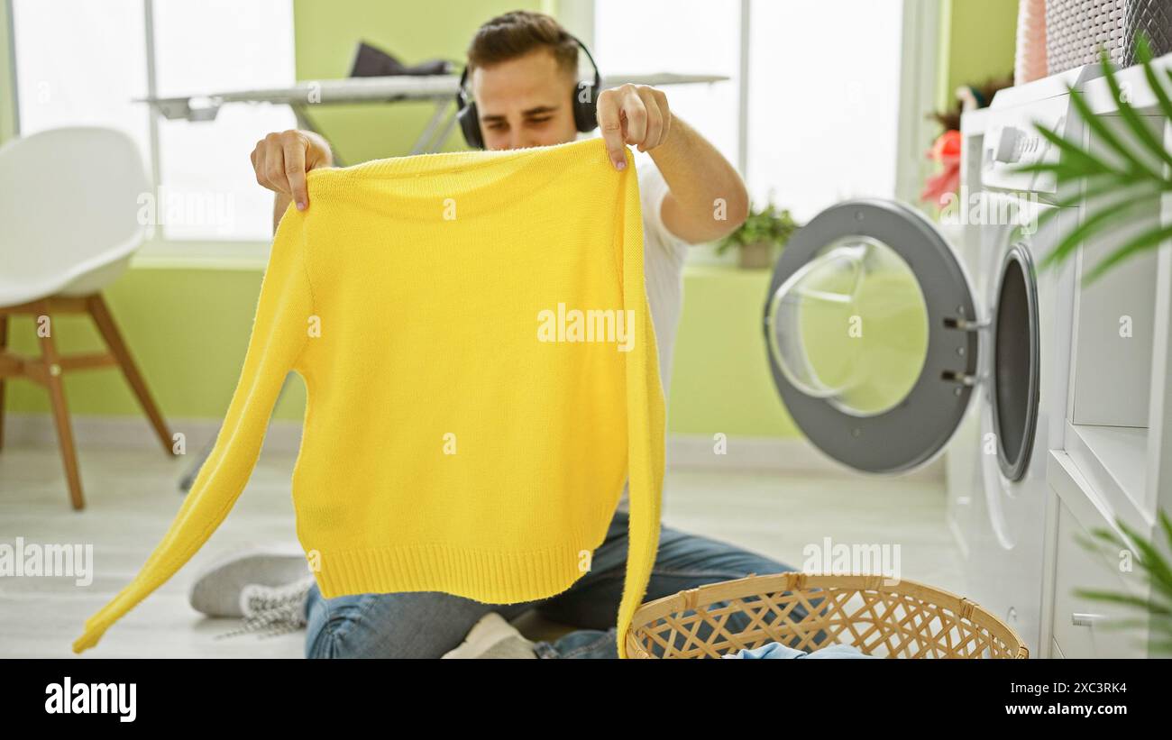 A young adult man inspects a yellow sweater while doing laundry in a ...