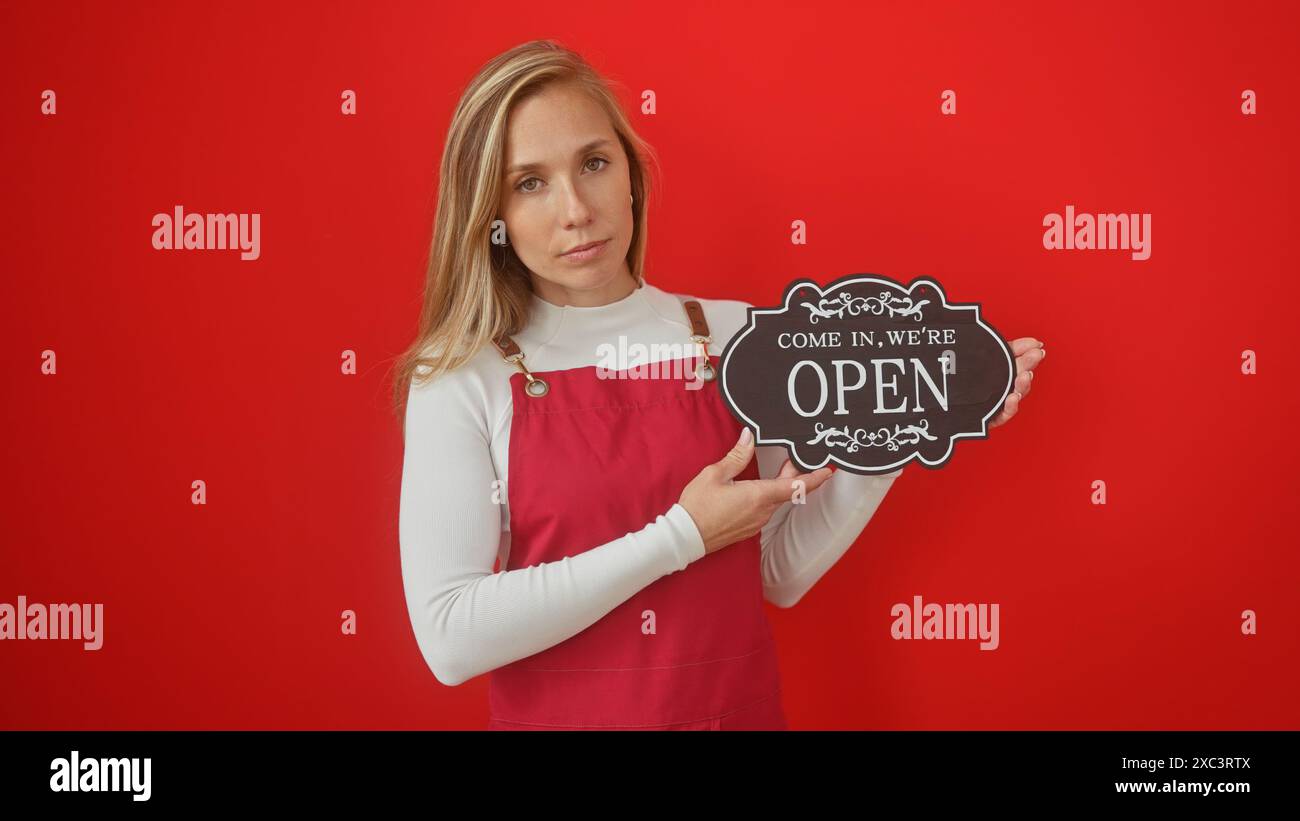 A confident young woman standing against a red background holds a 'come ...