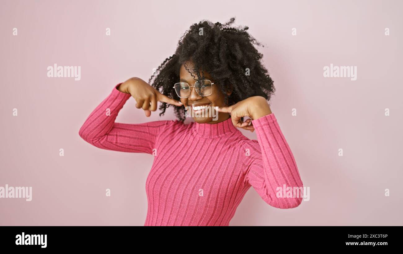 A happy black woman with glasses pointing to her smile indoors against ...