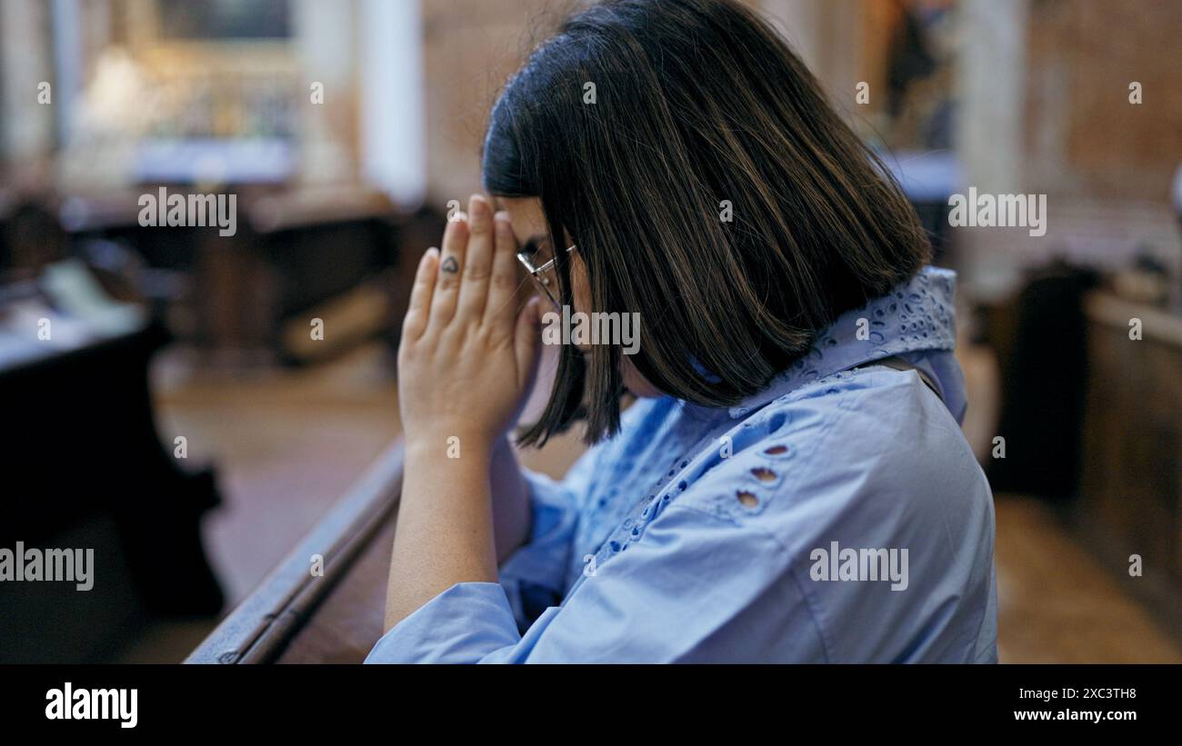 Young beautiful hispanic woman praying on a church bench at St. Karl ...