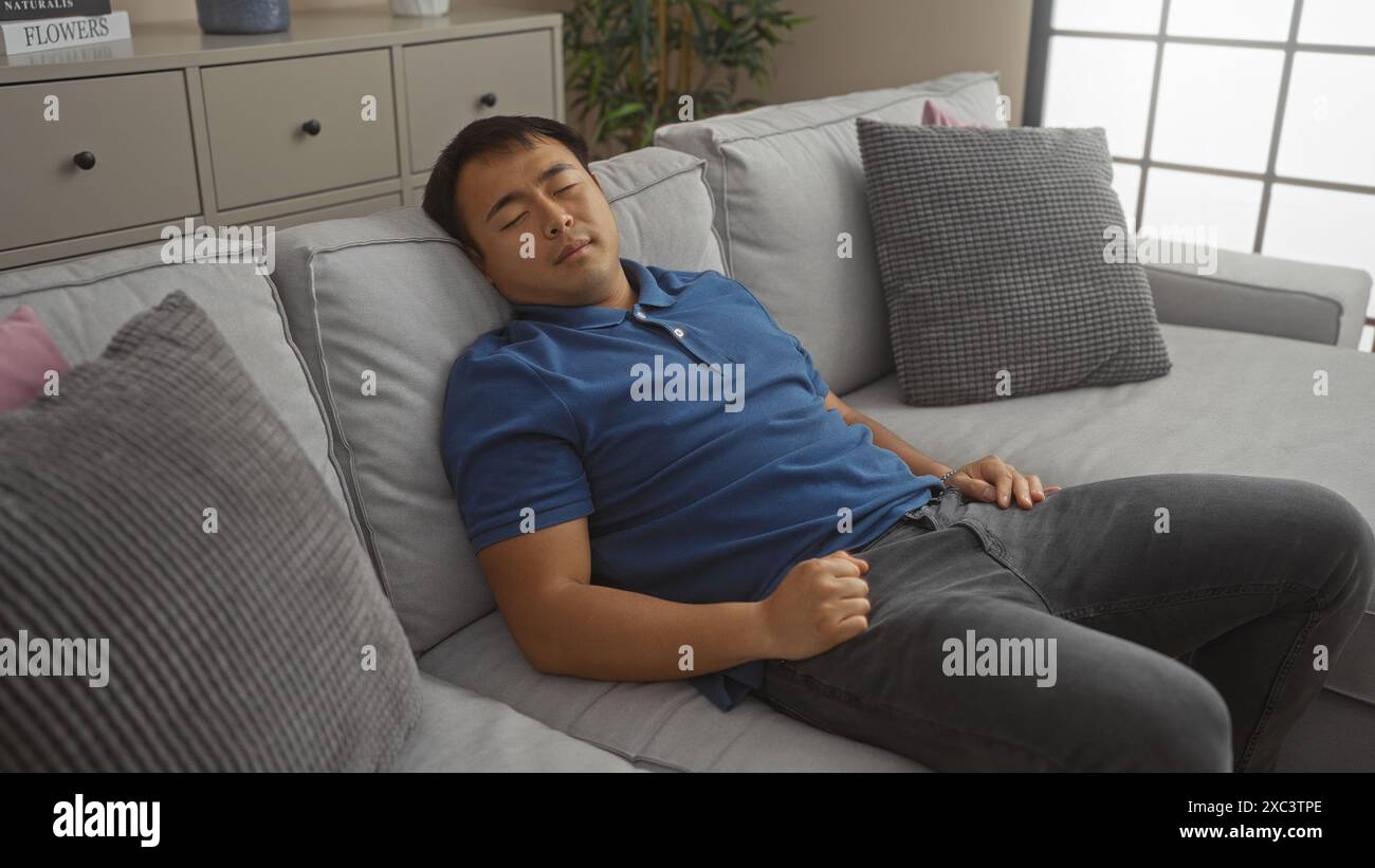 A young chinese man is sleeping on a couch in a modern living room ...