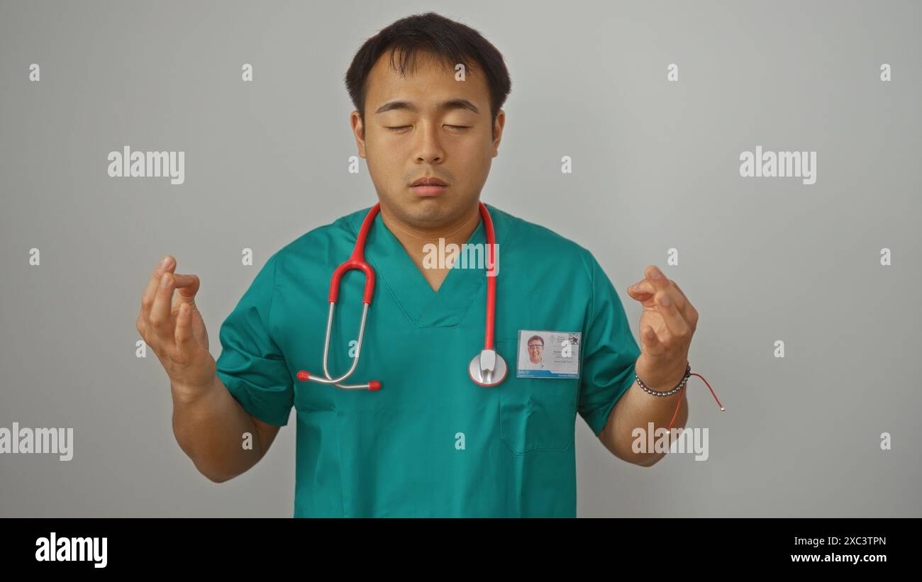 A young chinese male doctor in green scrubs meditates with closed eyes ...