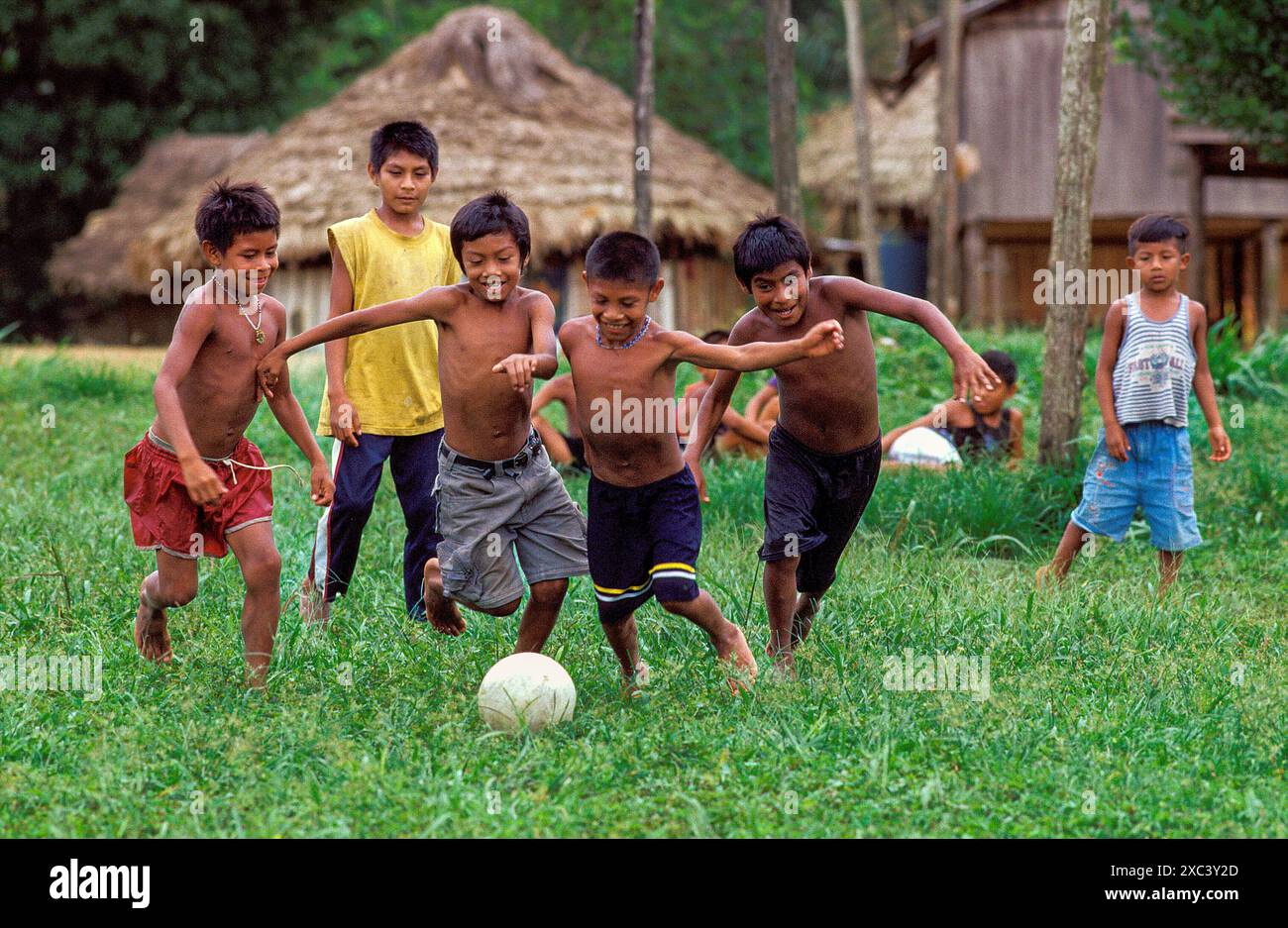 Suriname, boys of the Trio tribe play football on a field in front of ...