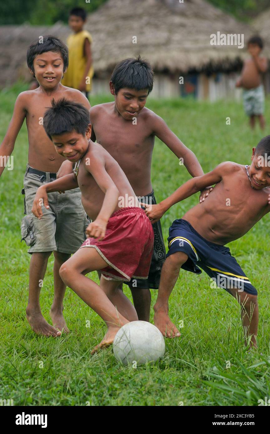 Suriname, boys of the Trio tribe play football on a field in front of ...