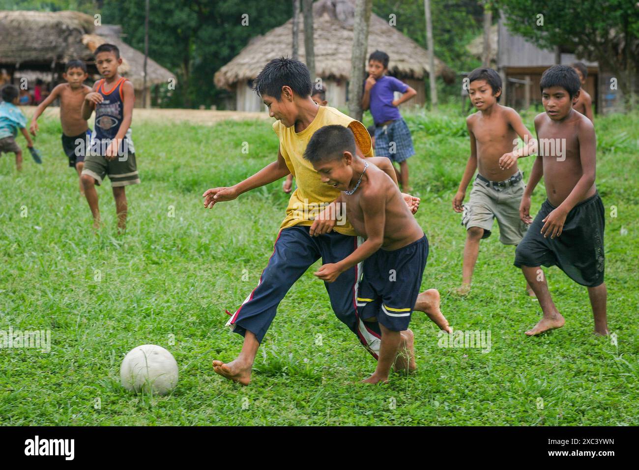 Suriname, boys of the Trio tribe play football on a field in front of ...