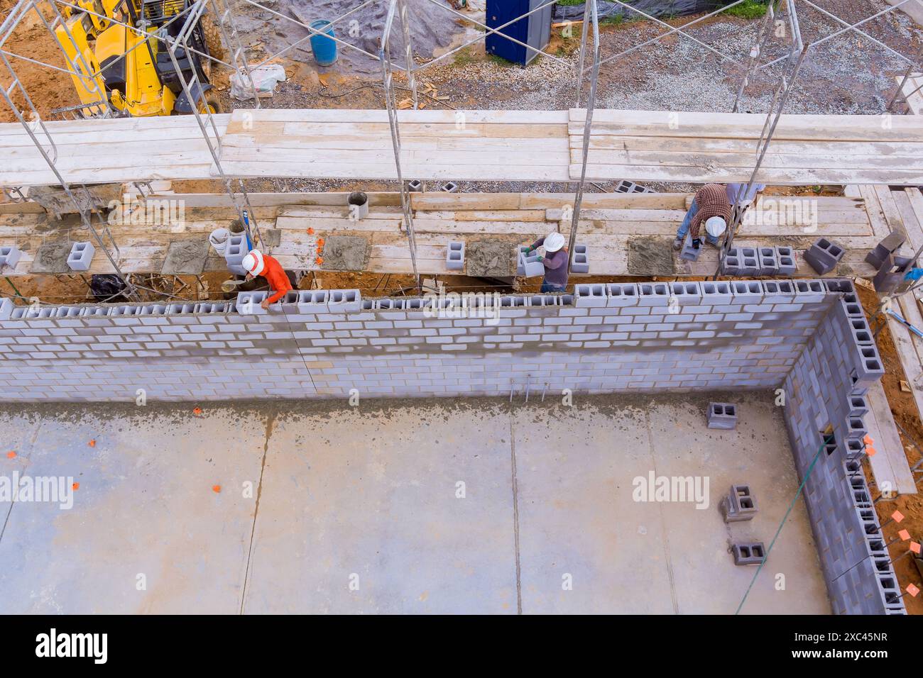 Working on scaffolding, mason constructs concrete wall with cement blocks Stock Photo - Alamy