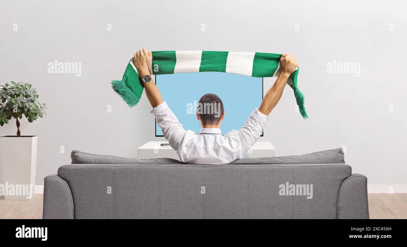 Man sitting on a couch and cheering with a scarf in front of a tv ...