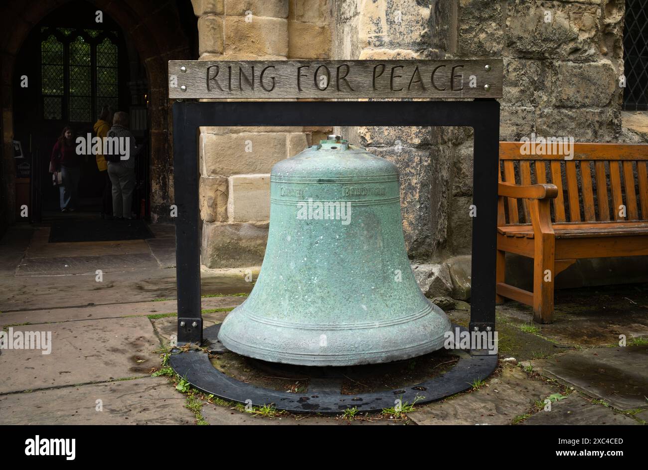 A large brass church bell with a sign reading "ring for peace" outside ...