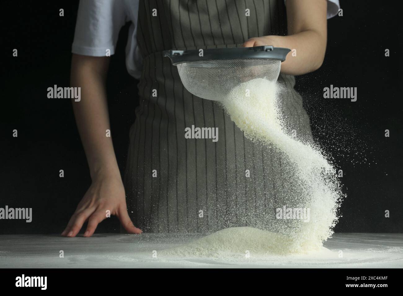 Woman sieving flour at table against black background, closeup Stock ...