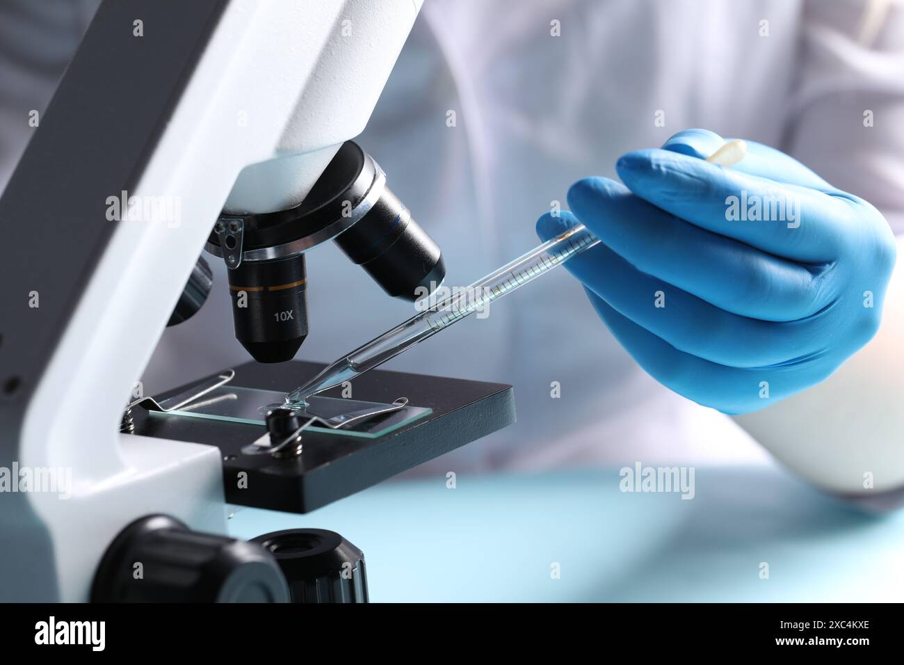 Doctor dripping liquid from pipette onto glass slide on microscope ...