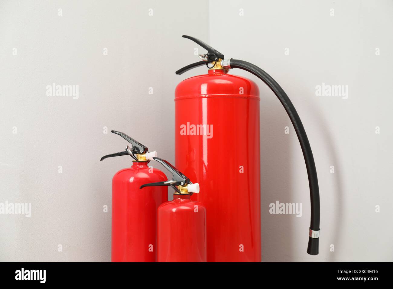 Three fire extinguishers near light grey wall Stock Photo - Alamy