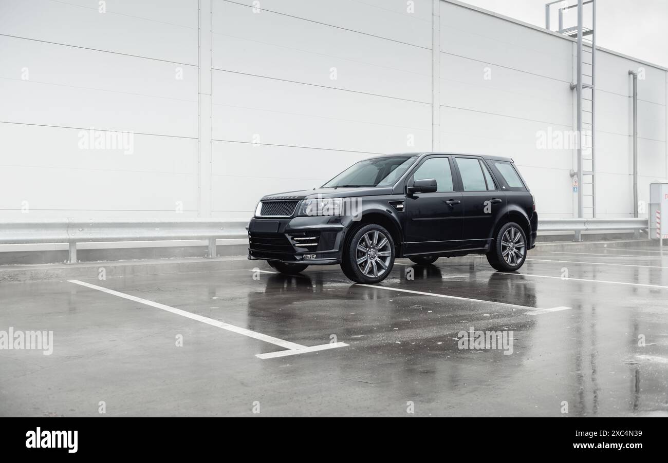Black Land Rover Freelander near light grey warehouse wall on a rainy ...