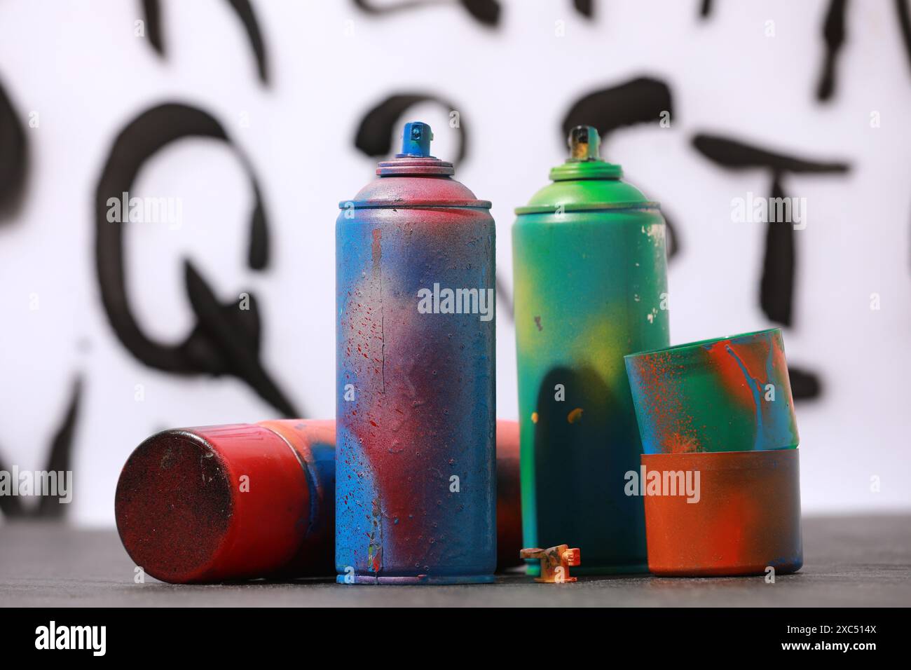 Many spray paint cans and caps on gray surface against white wall with ...