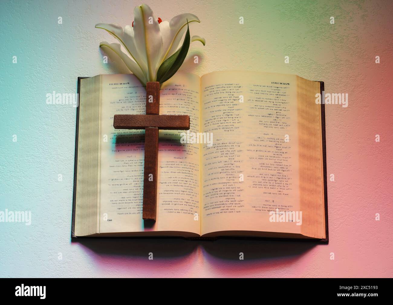 Wooden cross, Bible and lily flower on textured table in color lights ...