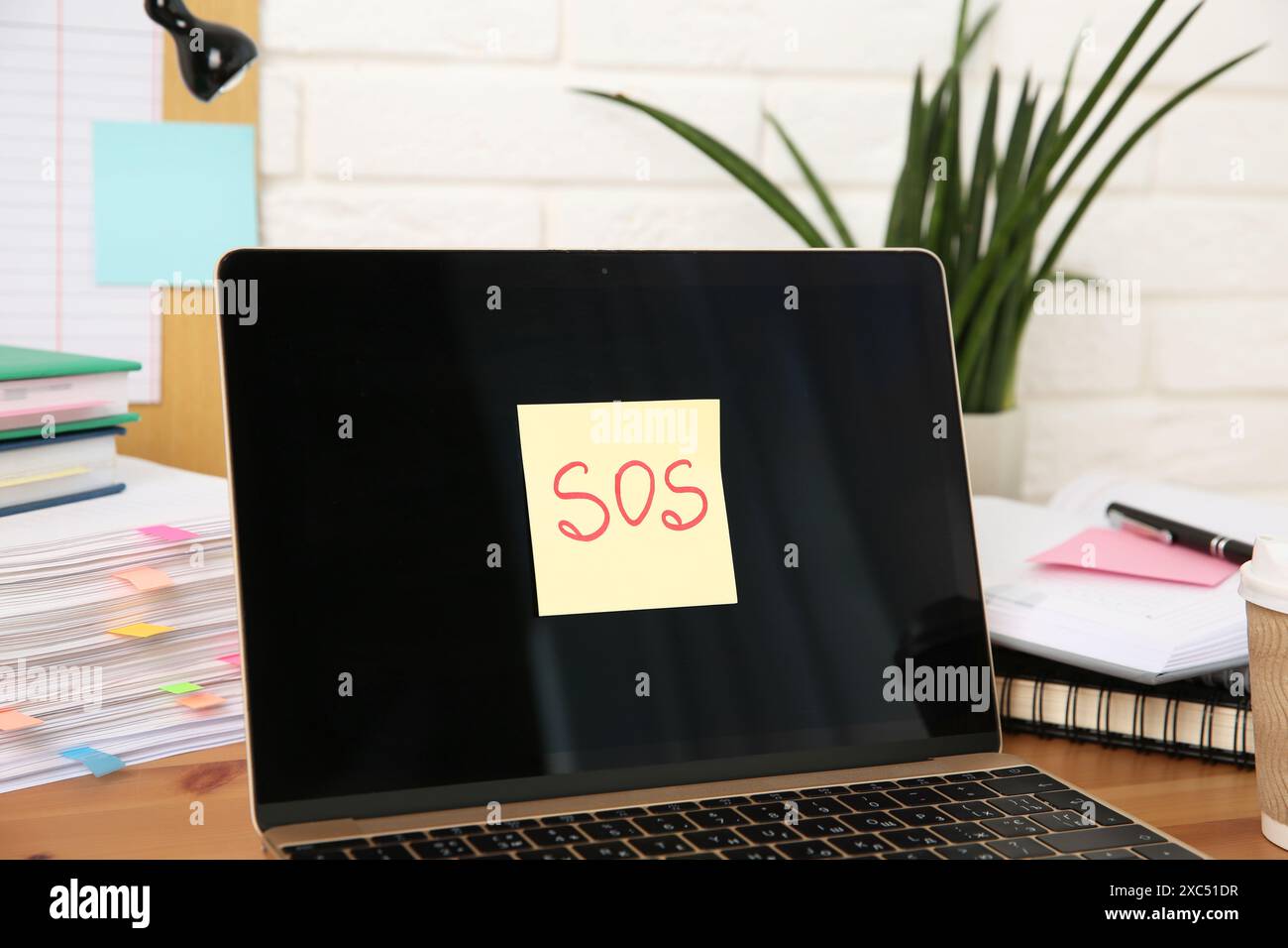 Note with word SOS, laptop and stationery on wooden table at workplace ...