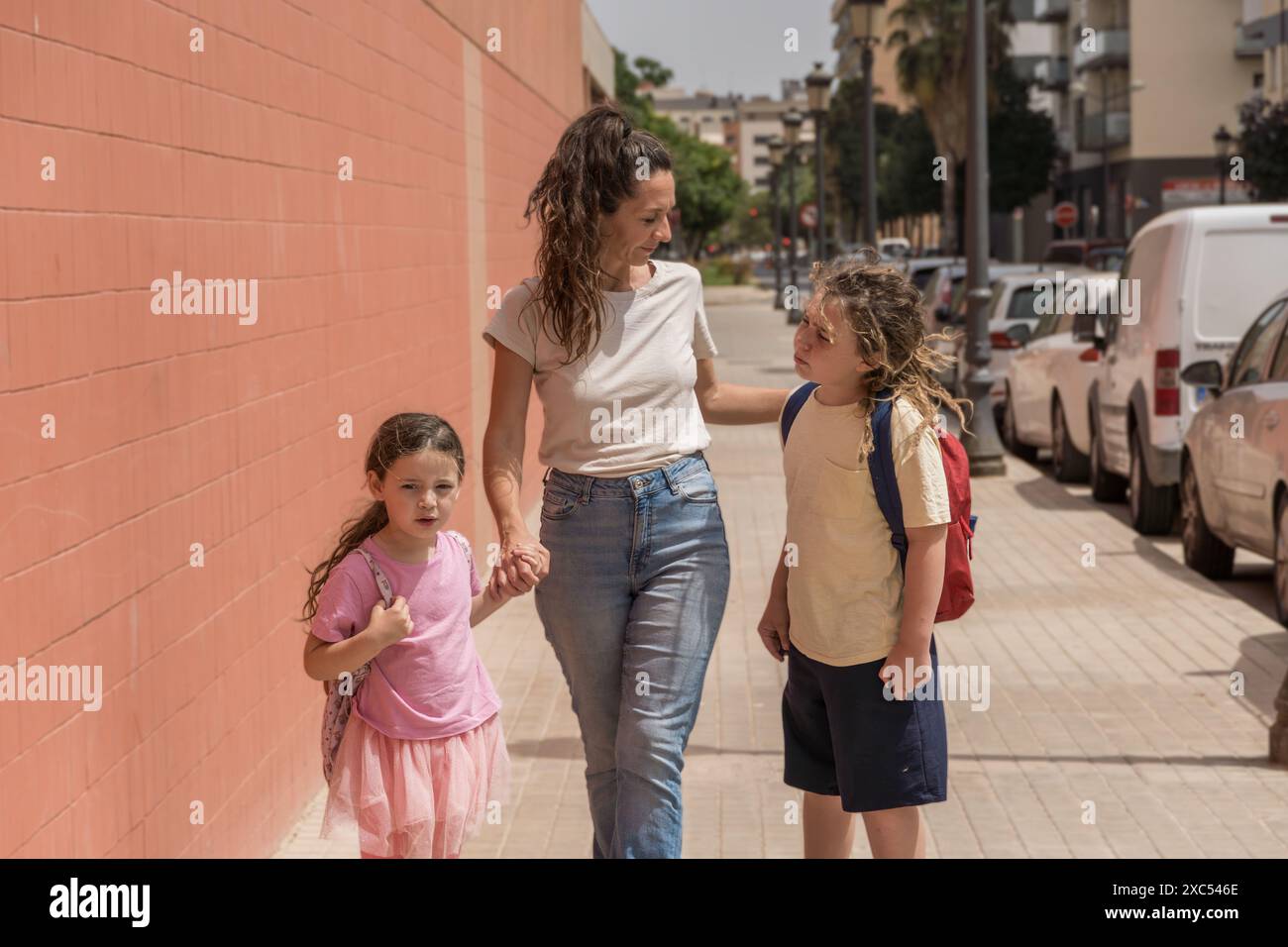 Young mom takes her kids with backpacks to school on a sunny day. Back ...