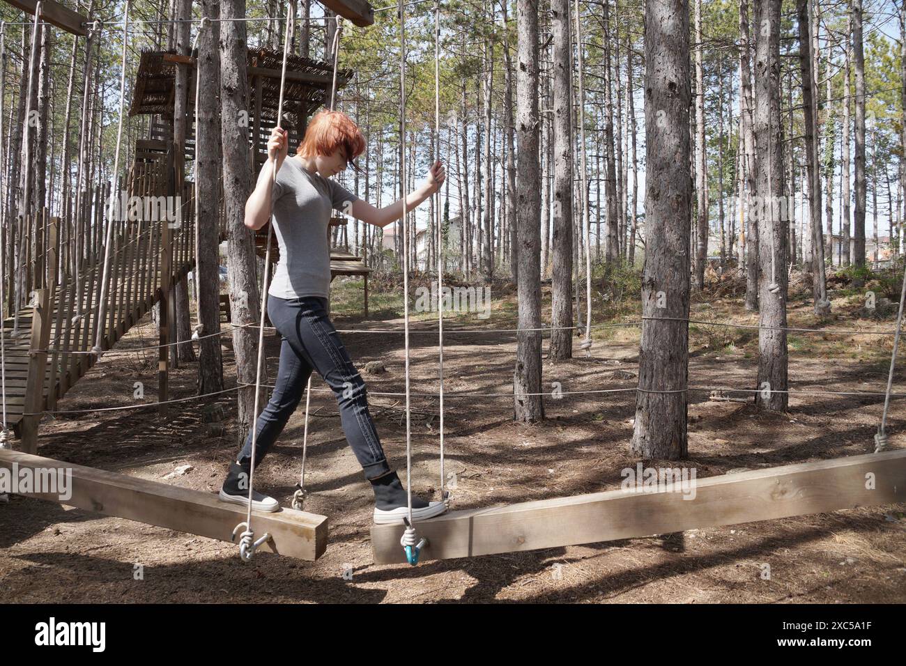 Rope training camp in the forest, a teenage girl walks on suspended ...
