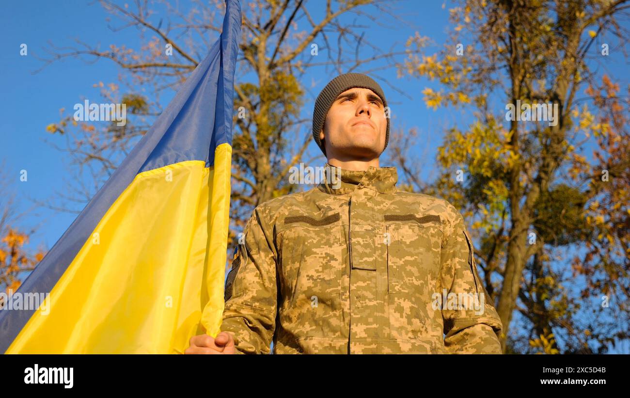 Ukrainian army man stands with national banner at countryside against ...