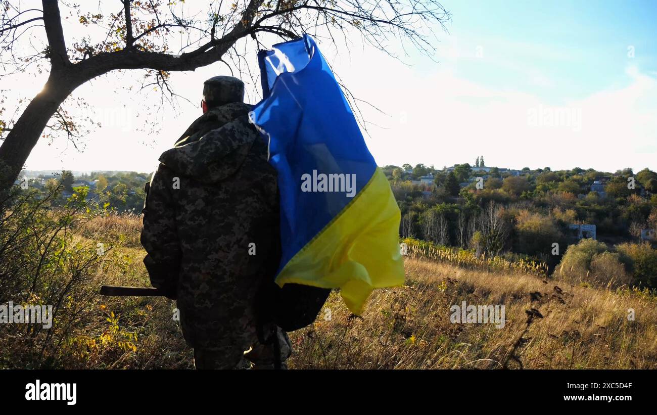 Young male military in uniform walks with waving flag of Ukraine at ...