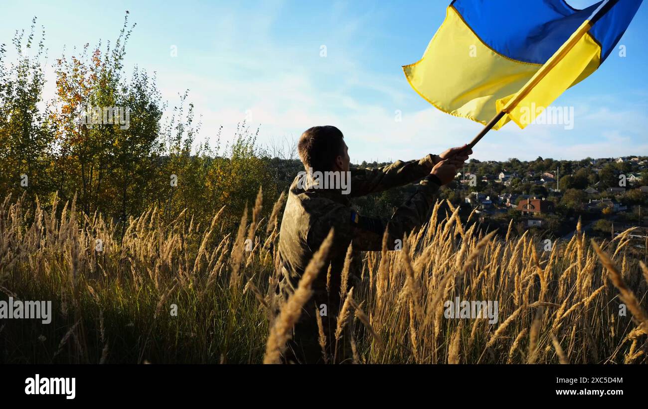 Male military in uniform waving flag of Ukraine at countryside. Young ...
