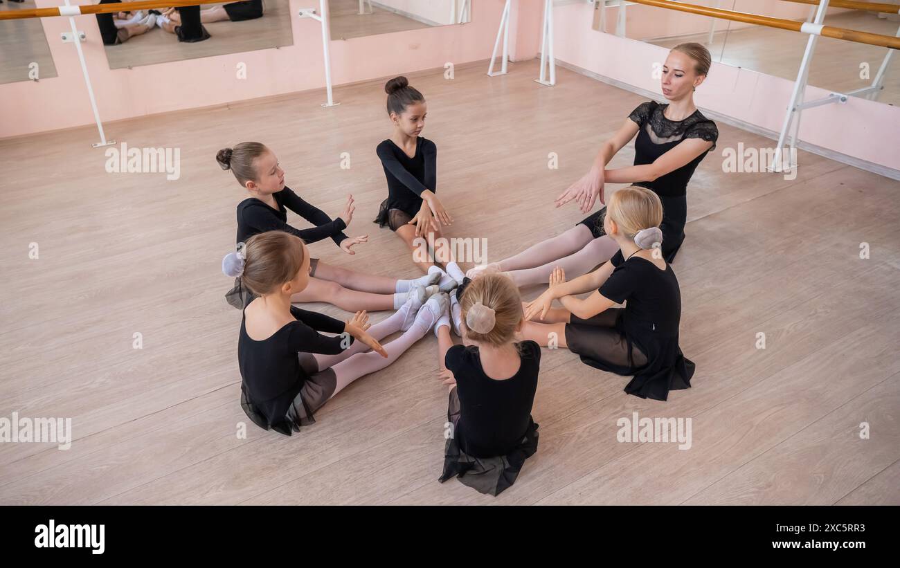 Caucasian woman and five little girls sit in a circle and do stretching ...