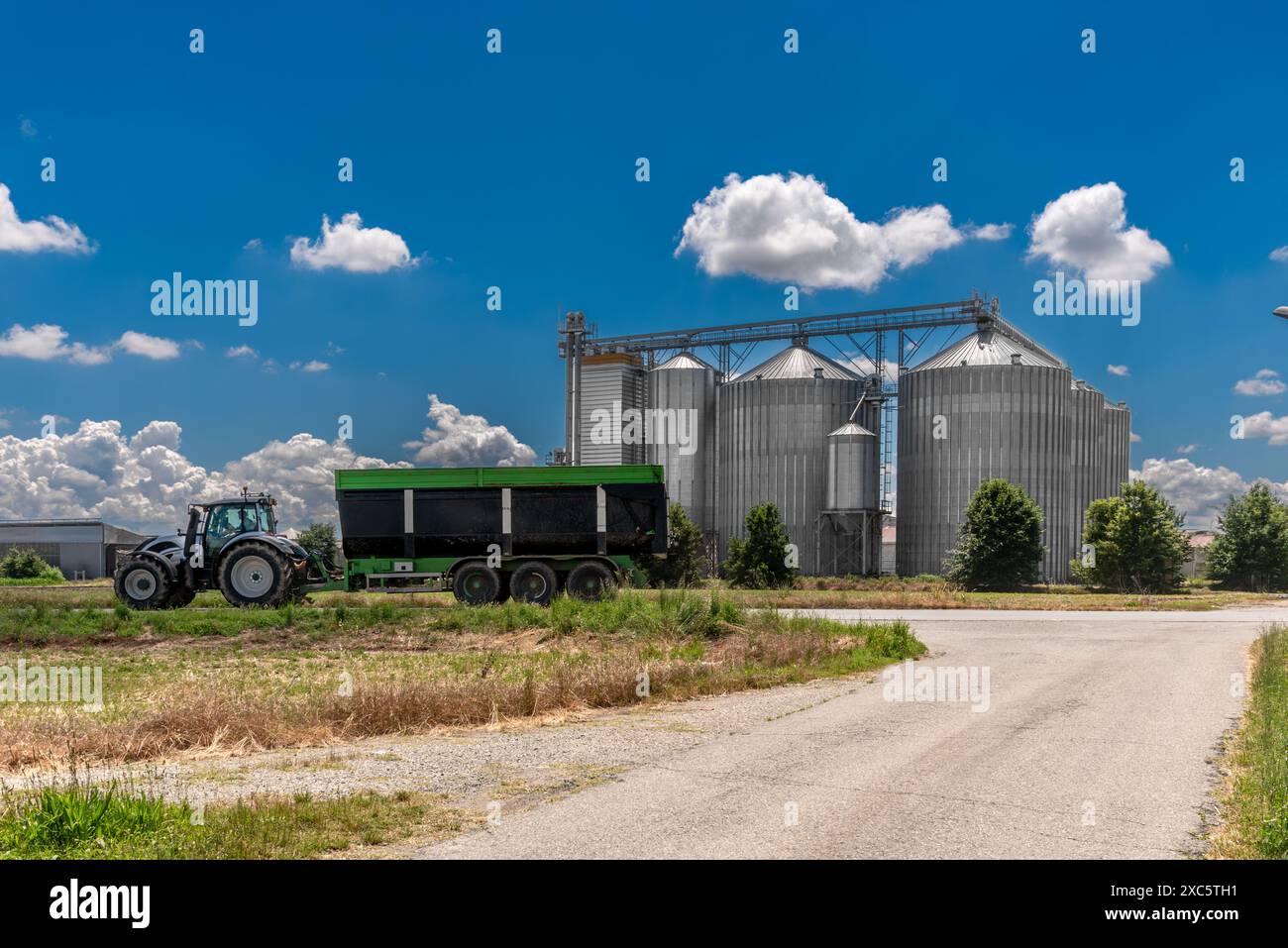 Tractor with grain harvesting trailer transits in front of steel grain ...