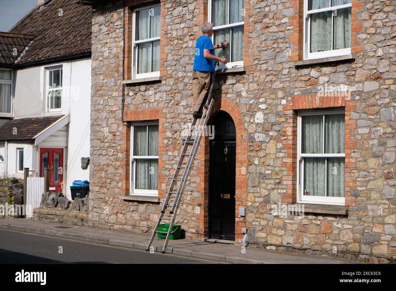 June 2024 - Mature man up a ladder alone cleaning windows beside a road ...