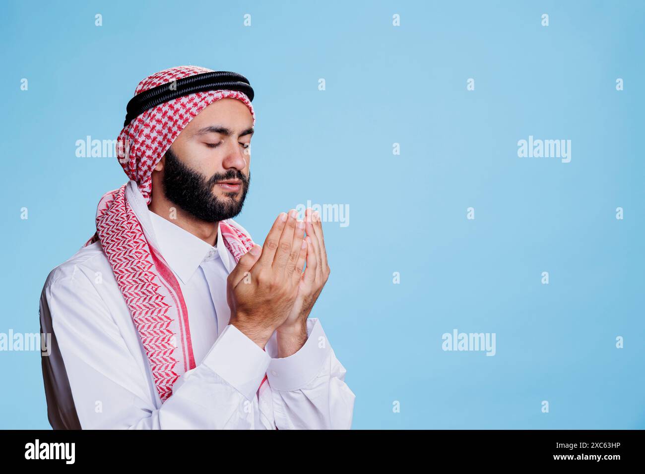 Man dressed in muslim clothes praying with open arms and closed eyes ...