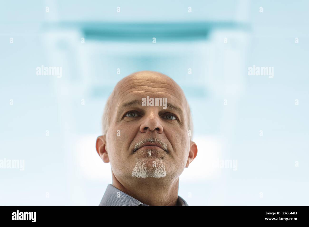 middle-aged man with a goatee and bald head looks slightly upwards with ...