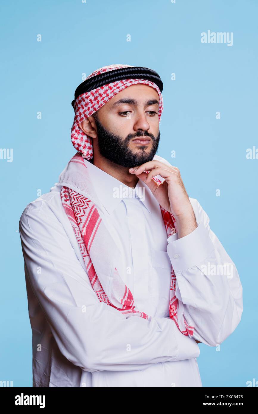 Pensive man wearing traditional muslim clothes rubbing chin and ...