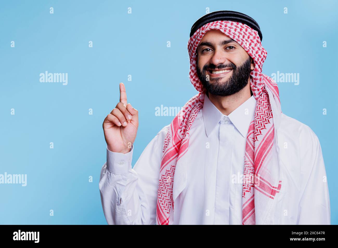 Smiling muslim man wearing arabic clothes pointing to upwards direction ...
