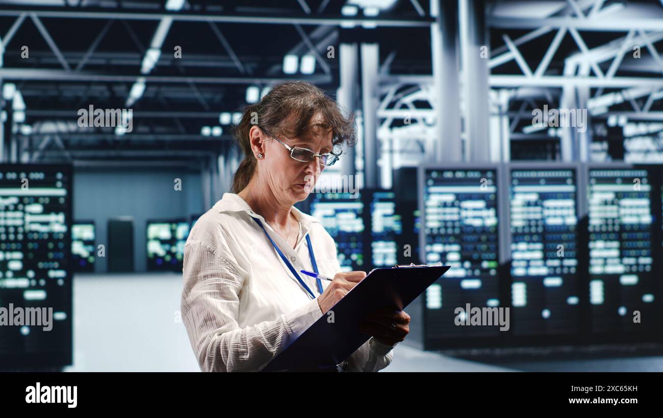 Aged IT admin in modern server room holding clipboard during data ...