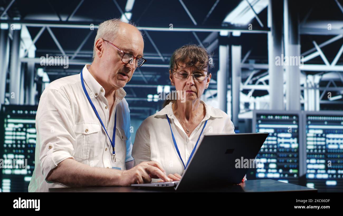 Octogenarian IT team looking around high tech data center, using laptop to crosscheck disaster ...