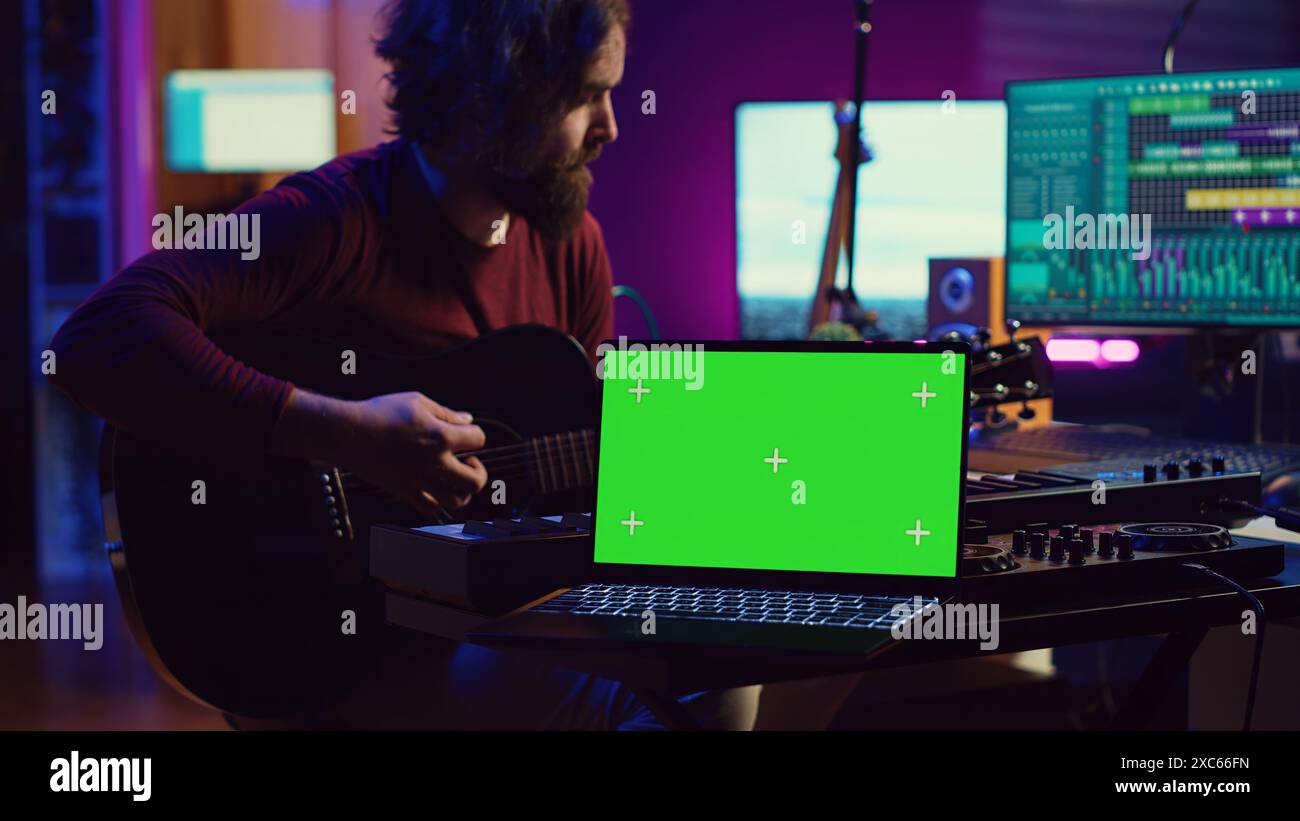 Guitarist playing his acoustic instrument next to greenscreen on laptop ...