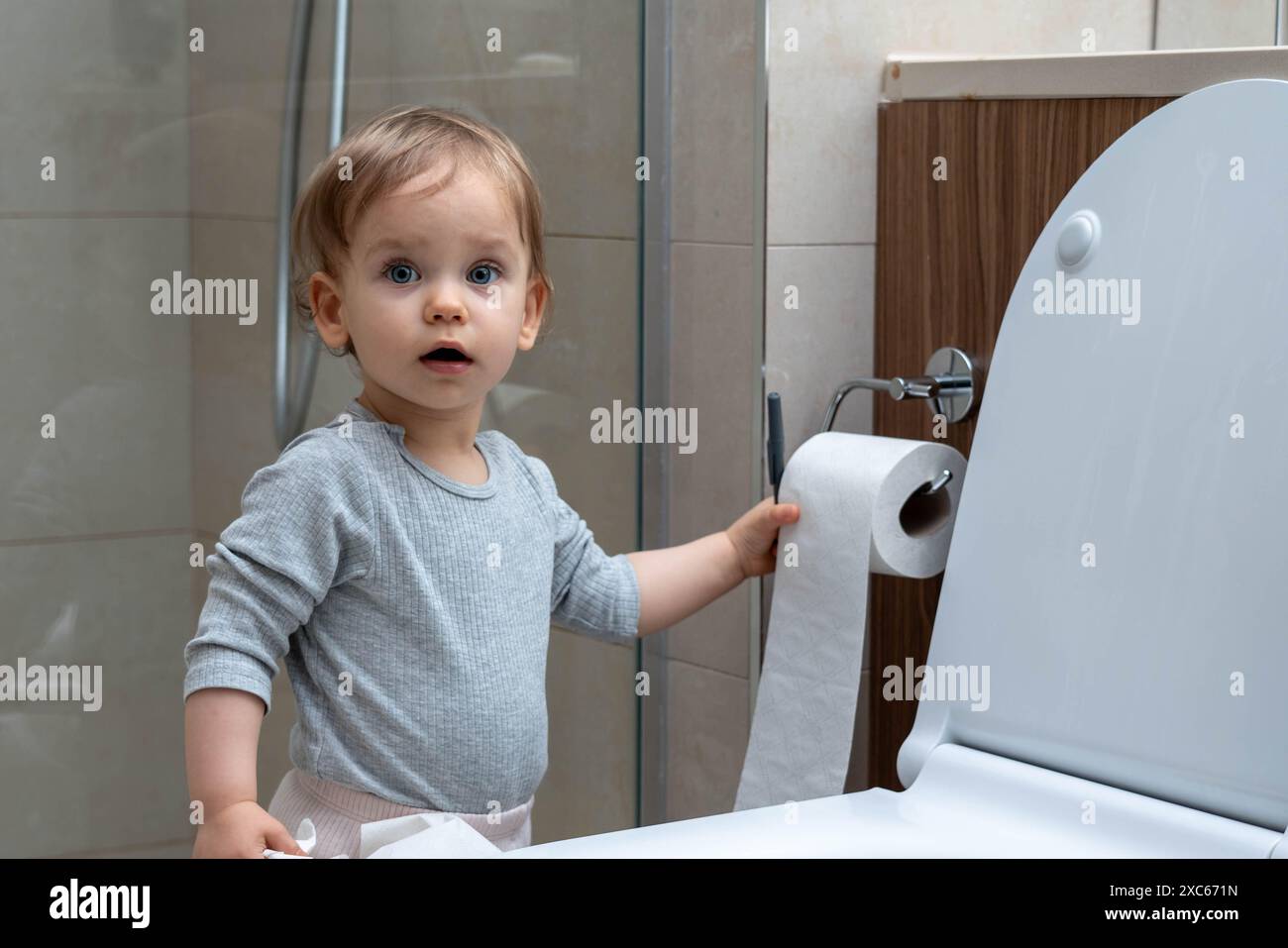 Toddler ripping up toilet paper in bathroom. Concept of naughty baby ...