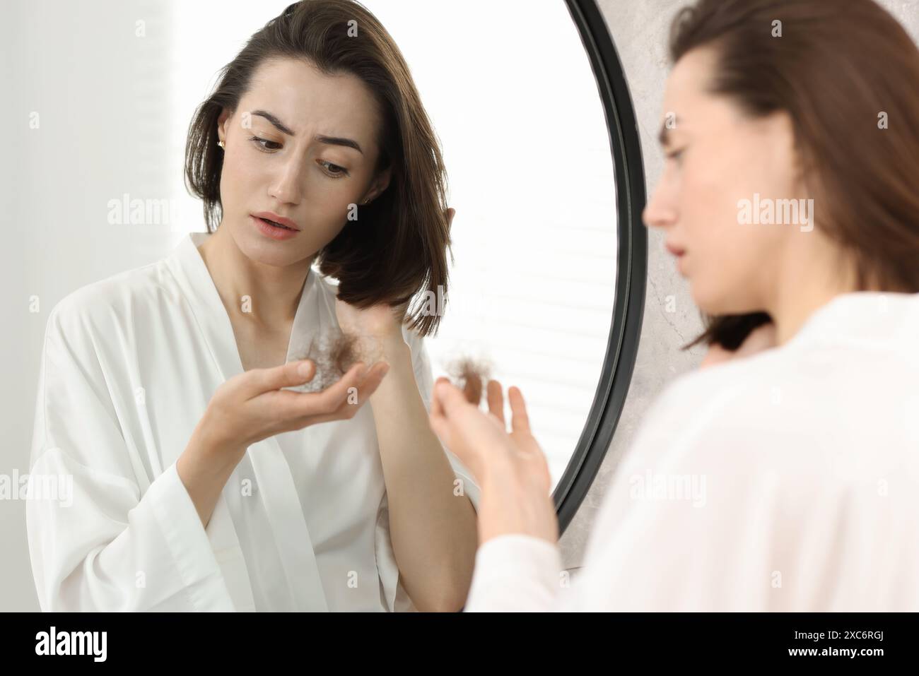 Sad woman holding clump of lost hair near mirror indoors. Alopecia ...