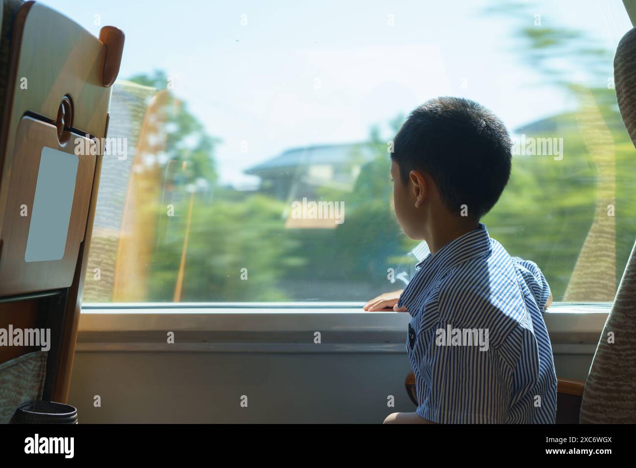 Asian young boy gazing out of a train window, captivated by the passing ...