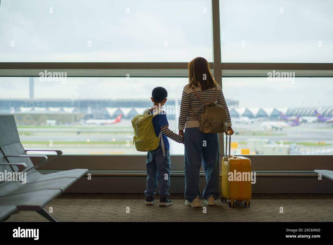 Asian mother and her young son standing side by side at an airport ...